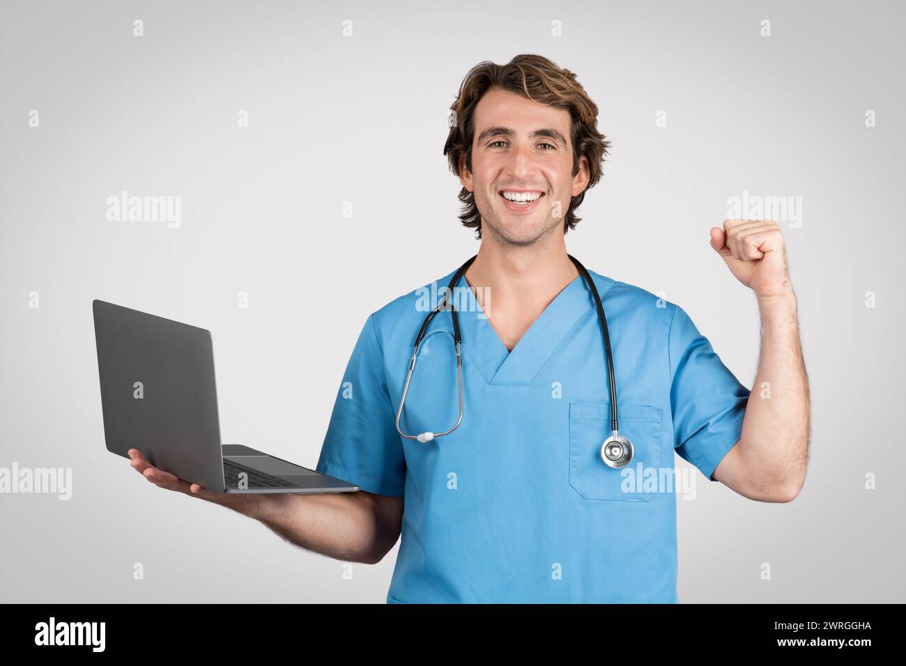 Cheerful male nurse with laptop celebrating success in blue scrubs ...