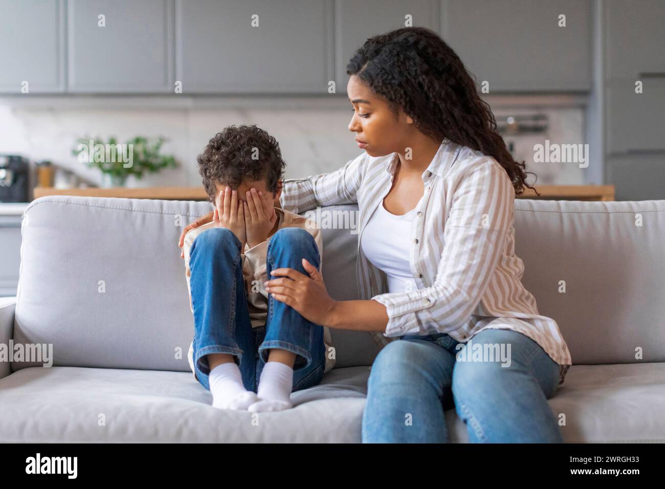 Caring young black mother comforting her distressed preteen son at home ...