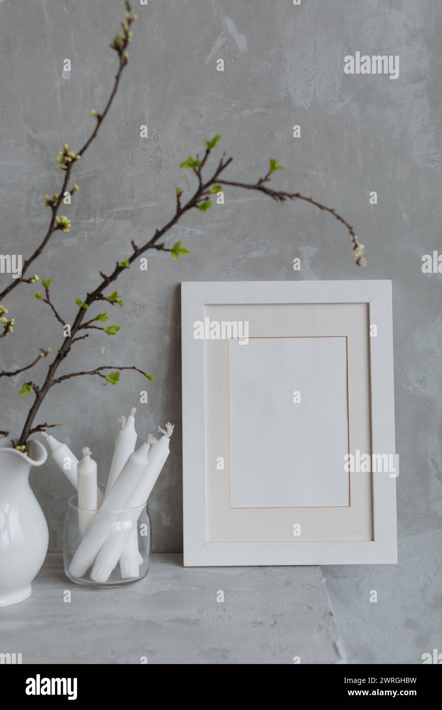 Blank picture frame next to cherry plum branches in a jug and candles ...