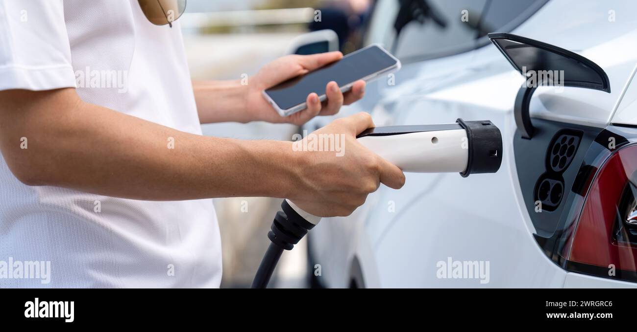 Hand insert EV charger plug into electric vehicle to recharge EV car, battery status display on ...
