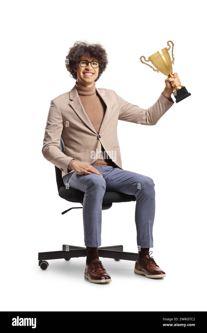 Young man sitting in an office chair and holding a gold trophy cup ...