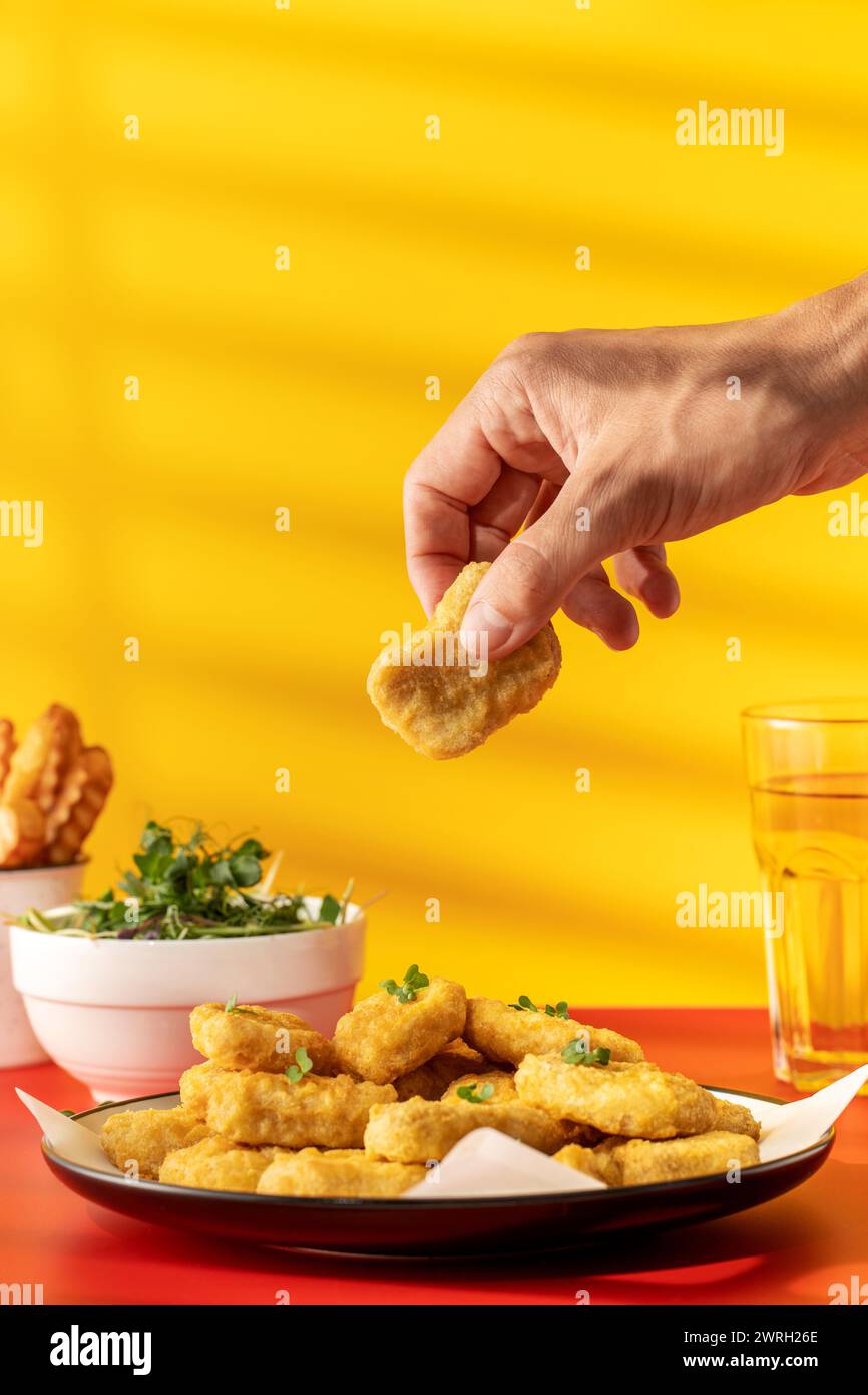 A person takes a golden chicken nugget from a plate on a colored ...