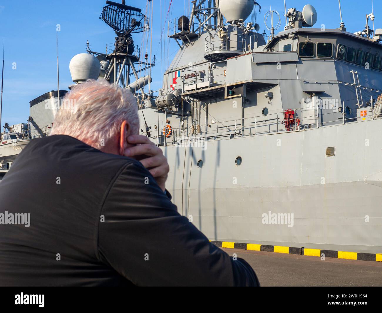 A local resident looks at a moored warship. Decks and weapons. Gray ...