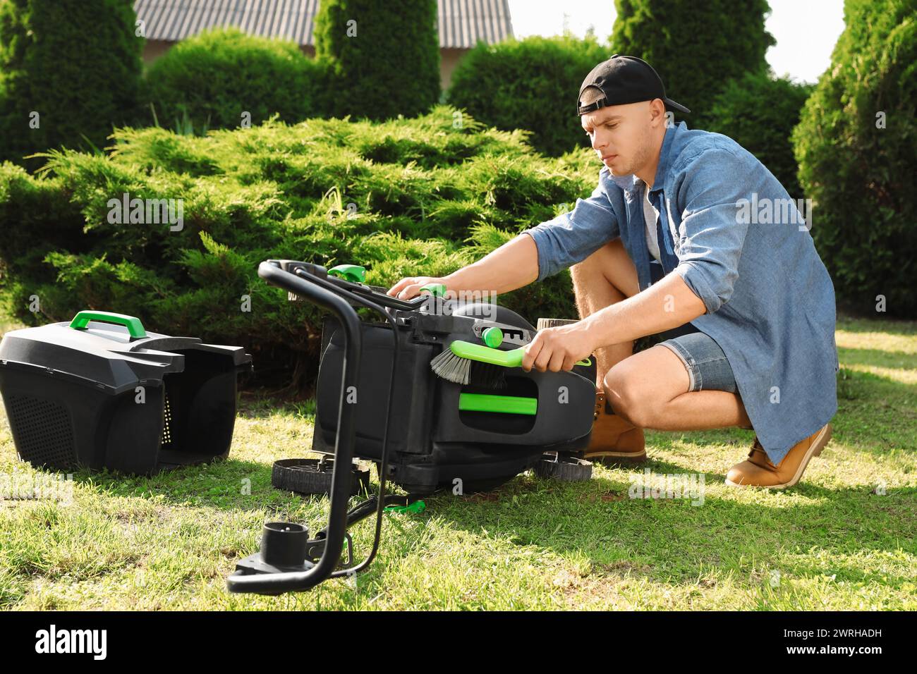 Young man cleaning lawn mower with brush in garden Stock Photo - Alamy