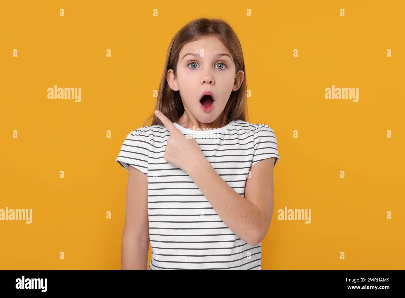 Surprised girl pointing at something on yellow background Stock Photo ...