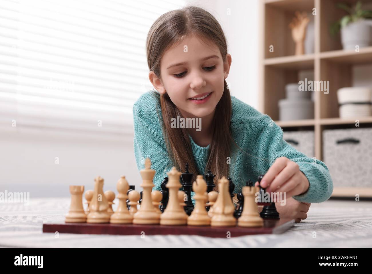 Cute girl playing chess on floor in room Stock Photo - Alamy