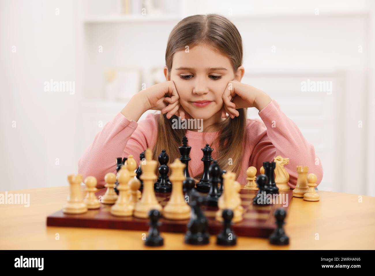 Cute girl playing chess at table in room Stock Photo - Alamy
