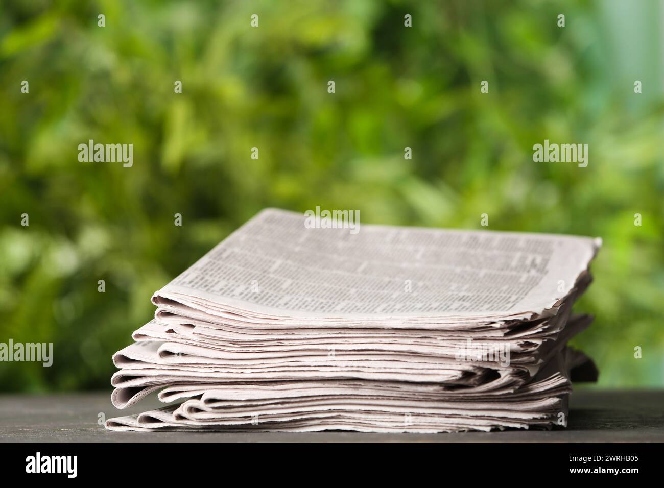 Stack of newspapers on grey table against blurred green background ...