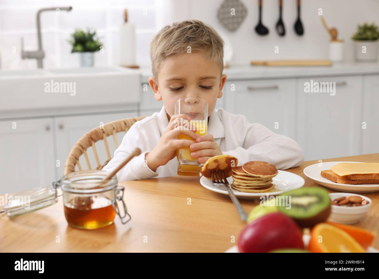 Breakfast time. Cute little boy drinking juice at table in kitchen ...