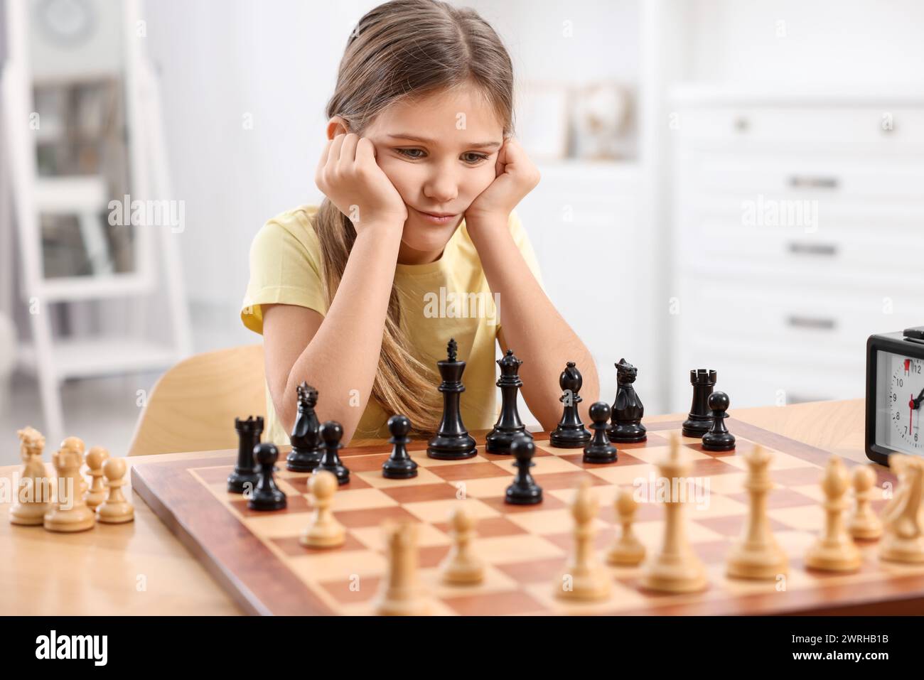 Cute girl playing chess at table in room Stock Photo - Alamy