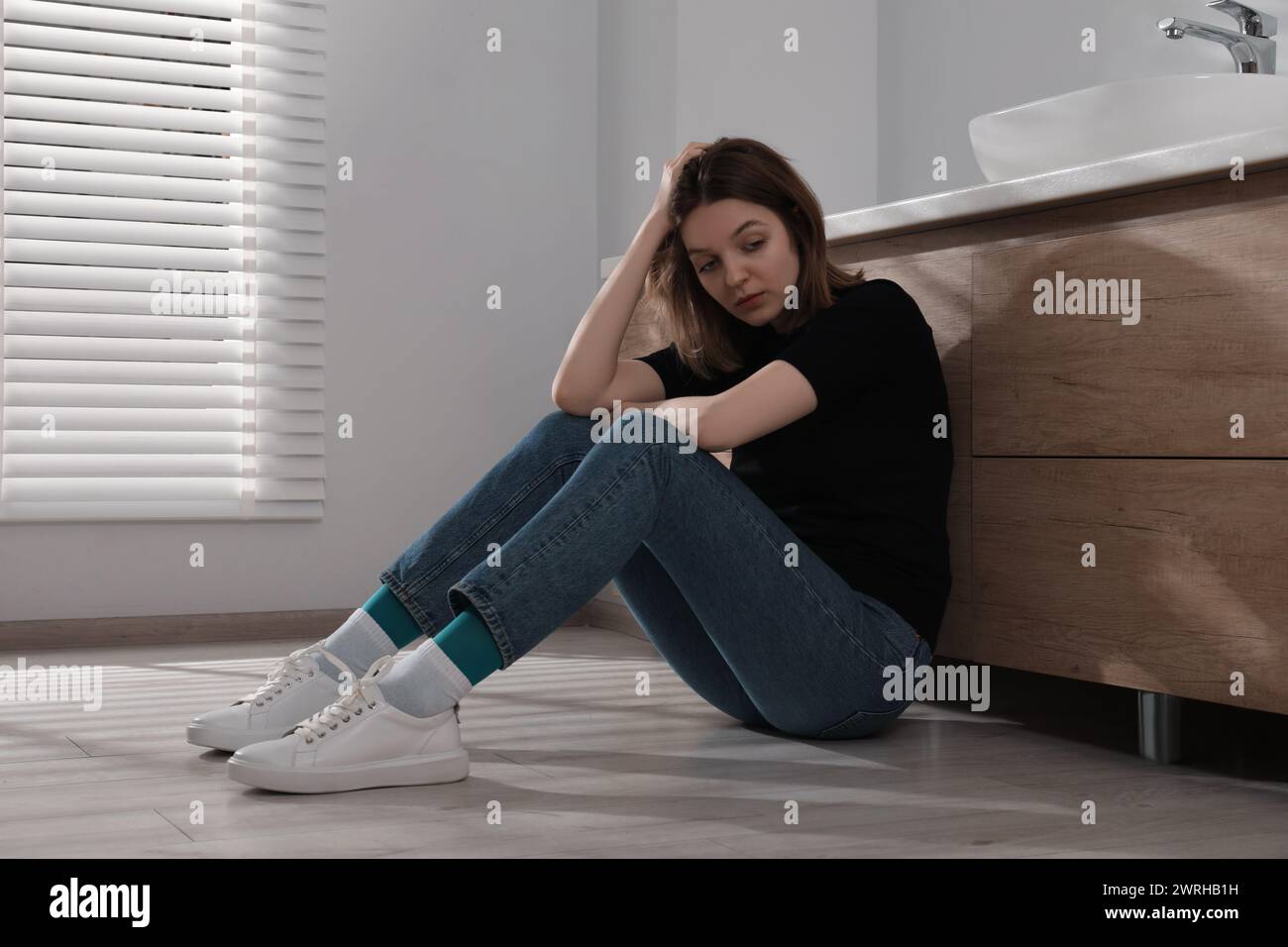 Sad young woman sitting on floor indoors Stock Photo - Alamy
