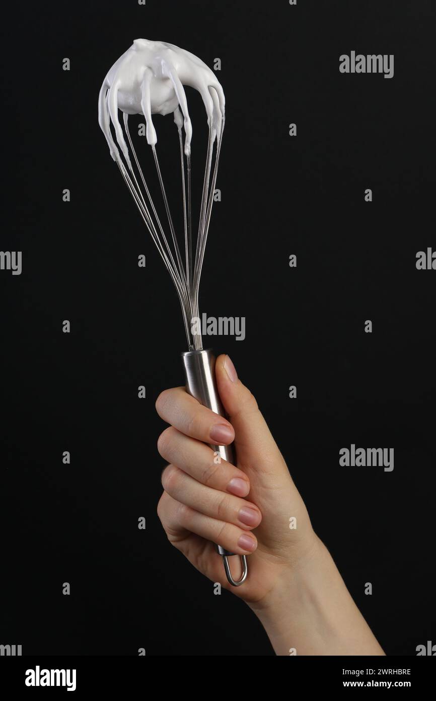 Woman holding whisk with whipped cream on black background, closeup ...