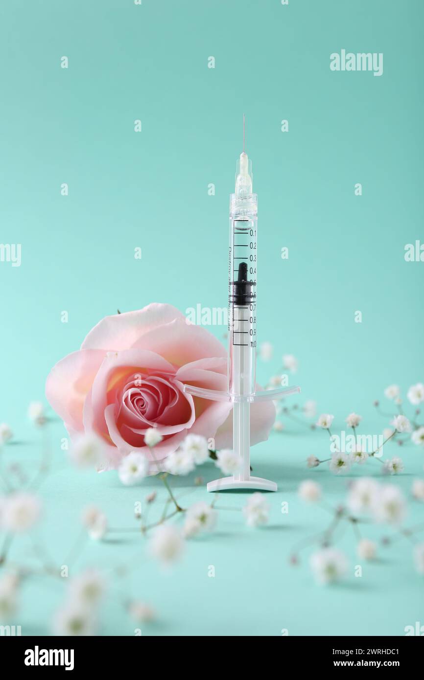 Cosmetology. Medical syringe, rose and gypsophila flowers on turquoise ...