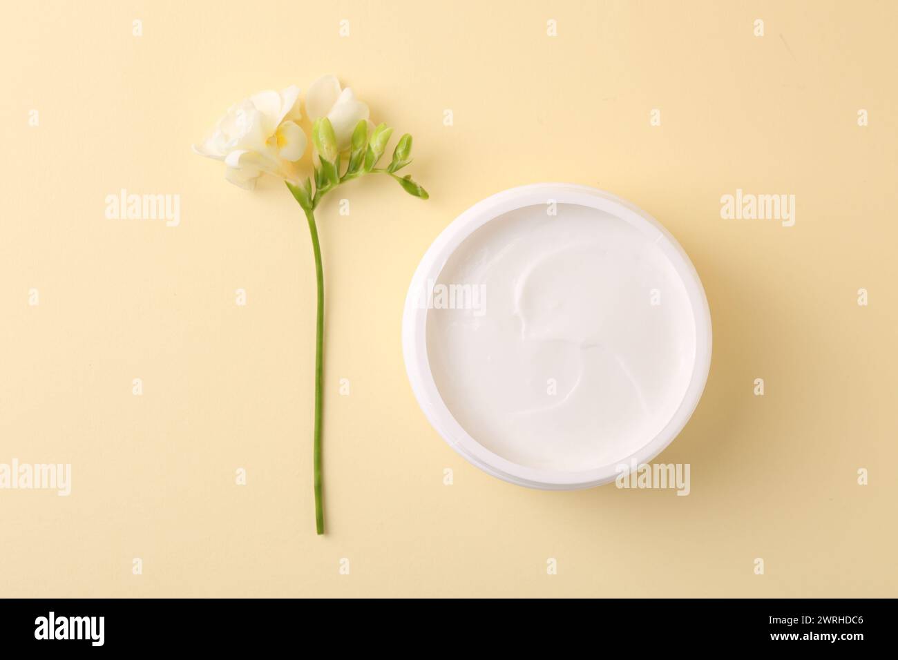 Moisturizing cream in open jar and freesia flower on beige background ...
