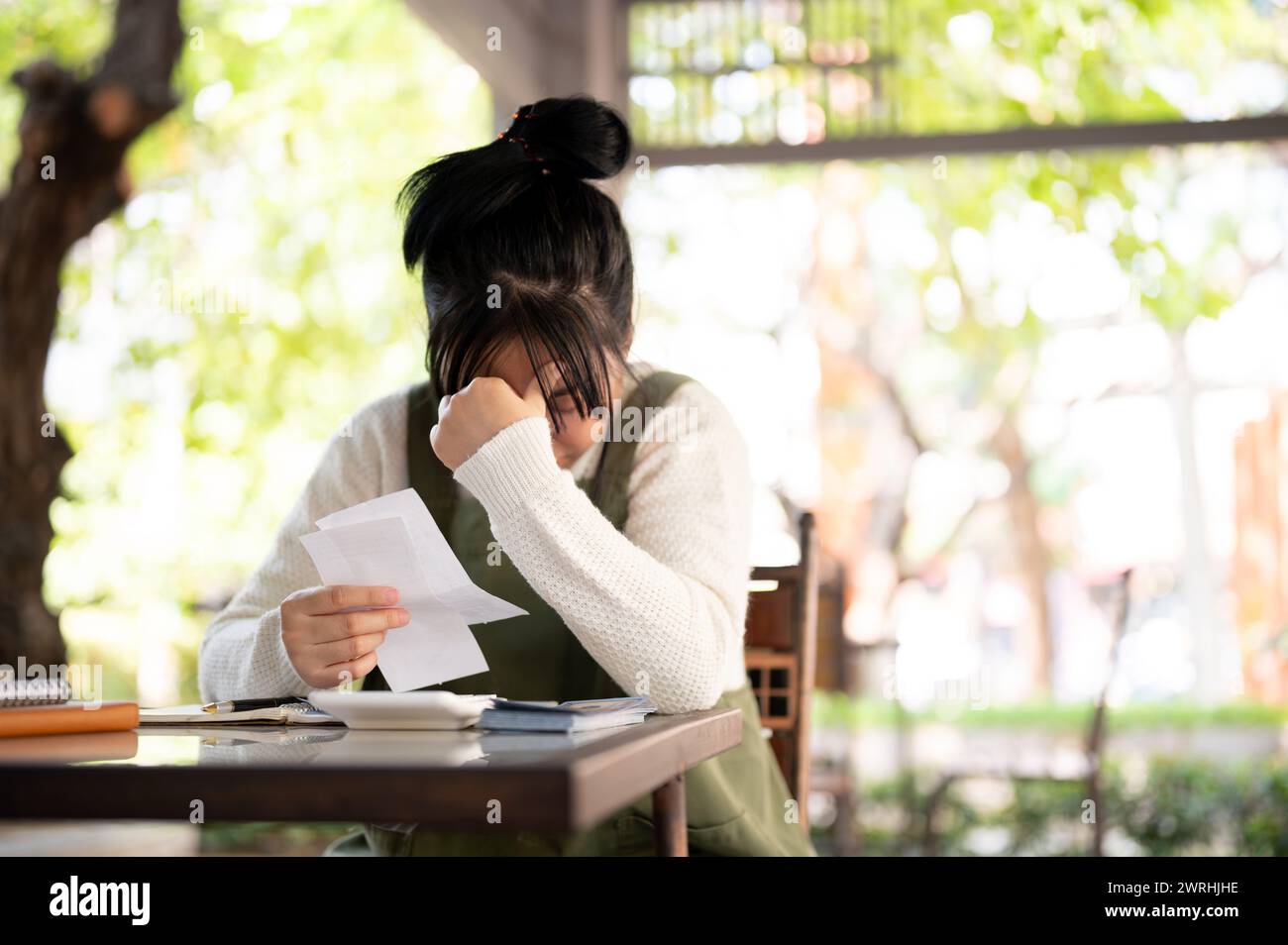 A stressed young Asian female small business owner is calculating bills ...