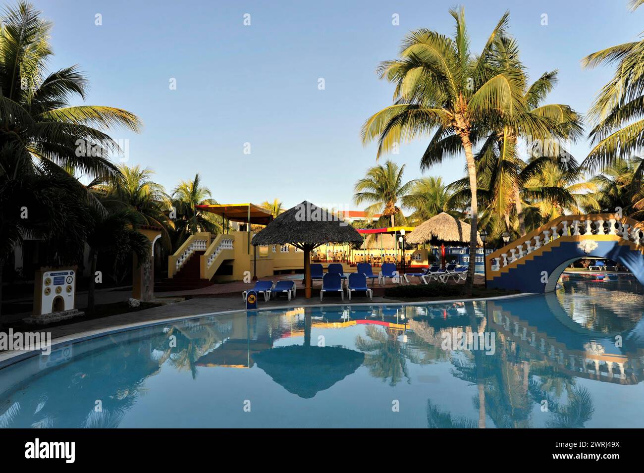 A quiet resort pool with sun loungers and palm trees at dawn, Trinidad ...