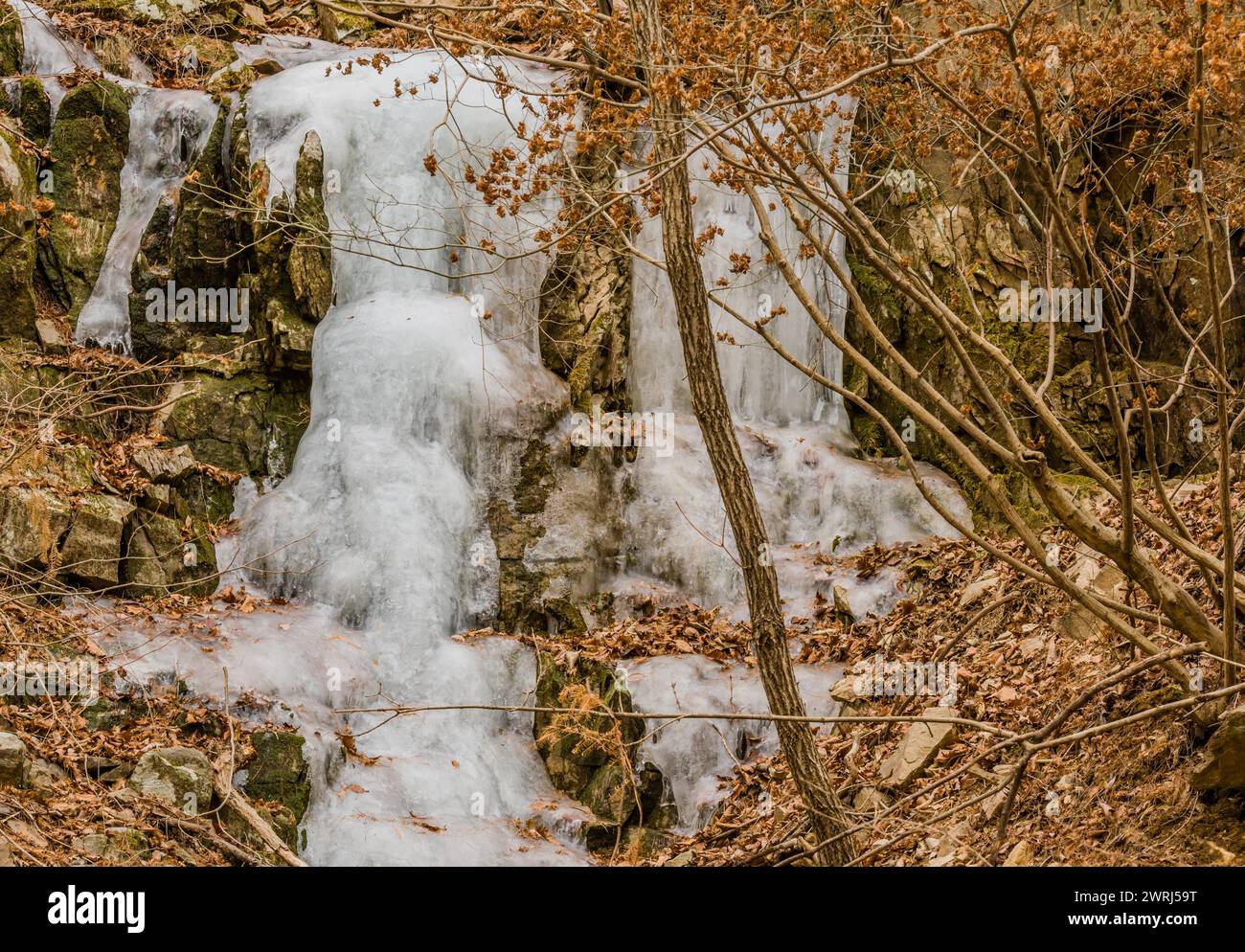Frozen waterfall on side of mountain with granite boulders behind a ...