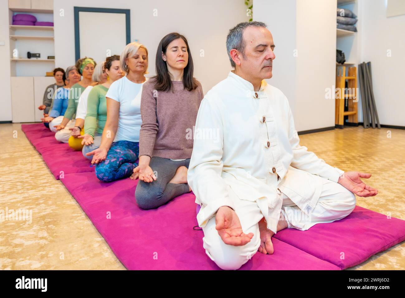 Yoga teacher leading a meditation in a community sitting on mat with ...