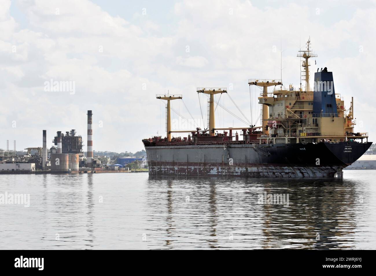 Large cargo ship in the harbour with cranes and factory buildings in ...