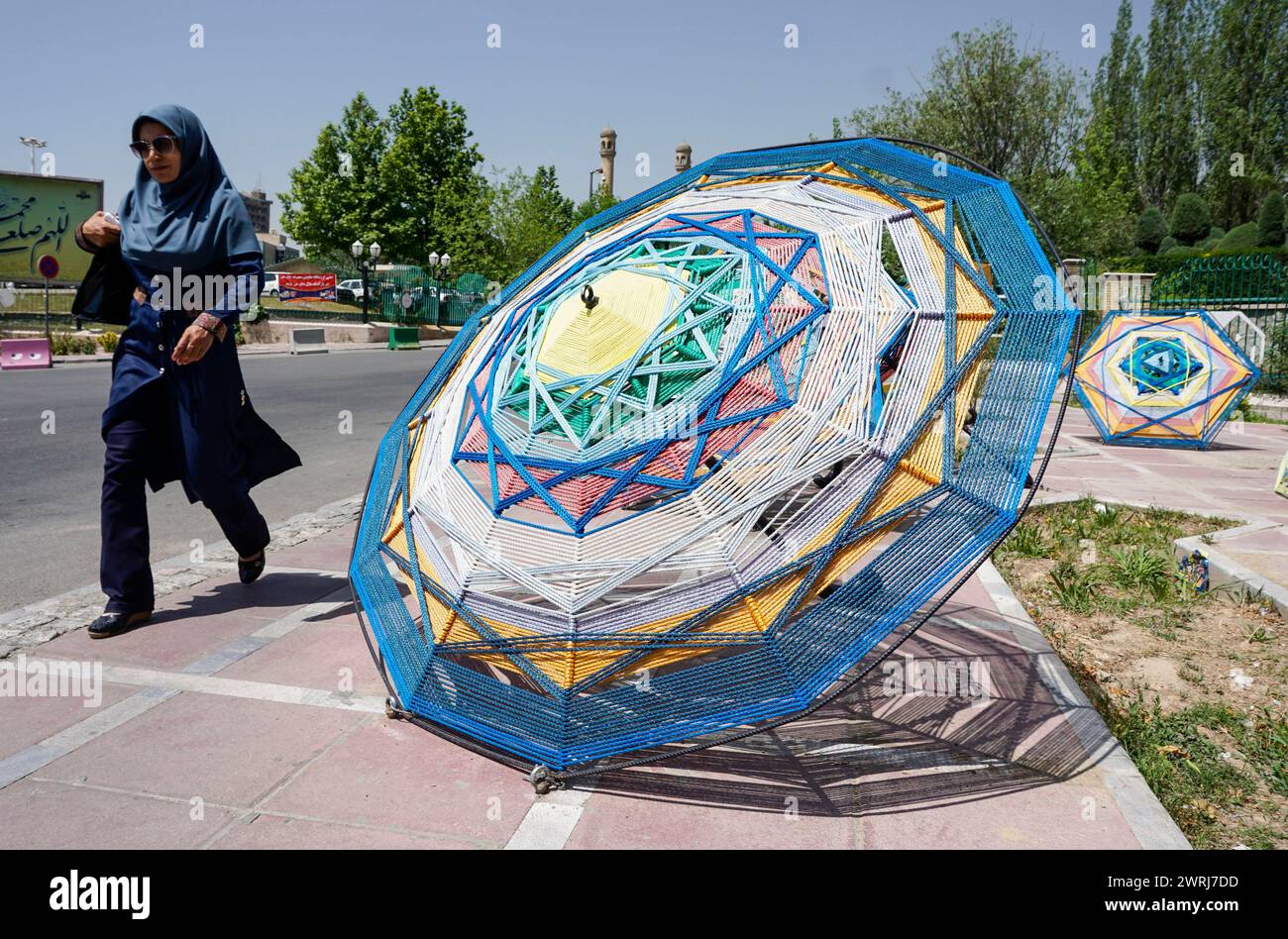 A woman walks past large umbrellas lying on the pavement in Tehran. The ...