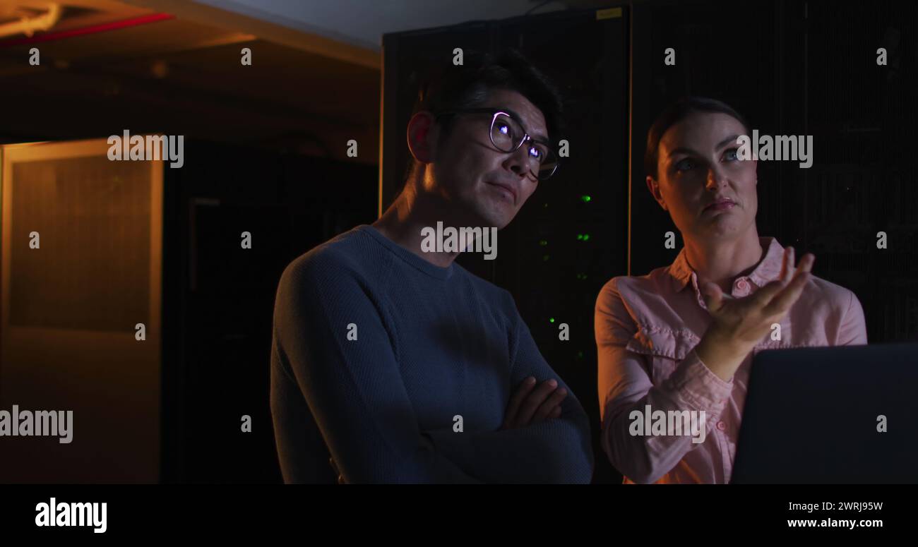 Caucasian woman and Asian man review data in a dim server room Stock ...