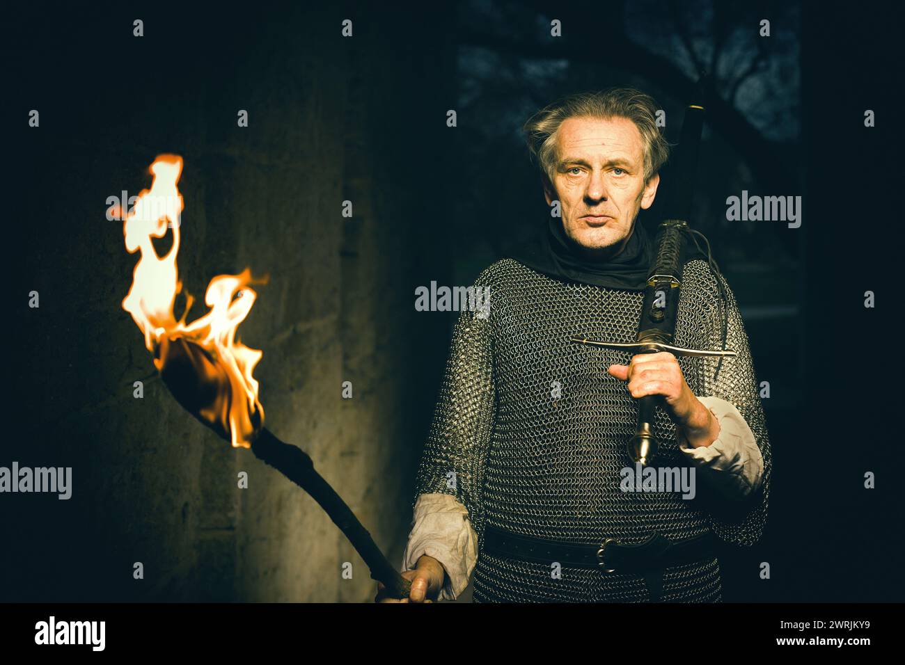 Medieval infantry armed man on guard in castle gateway with lit torch ...