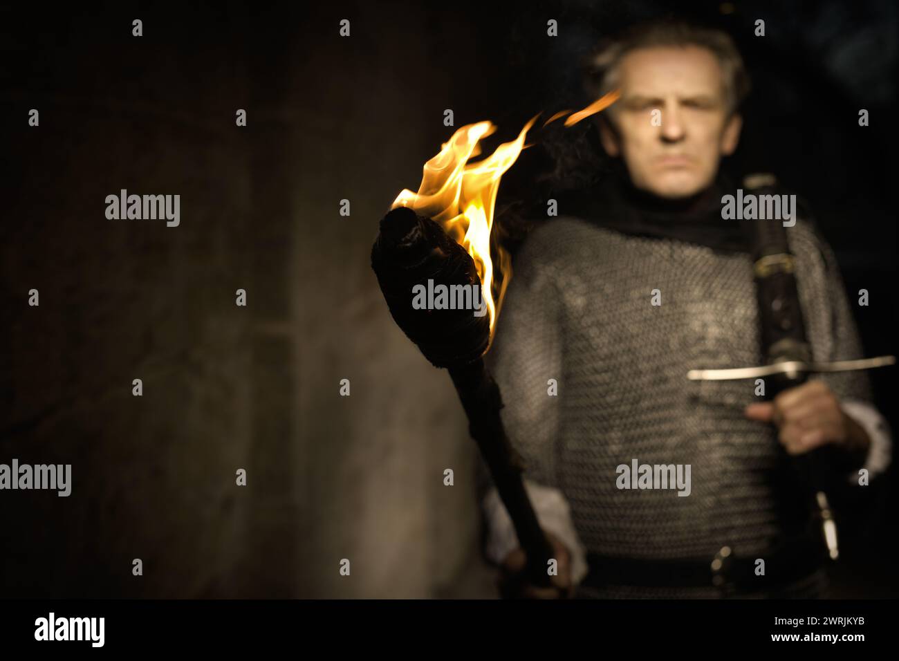 Medieval infantry armed man on guard in castle gateway with lit torch ...