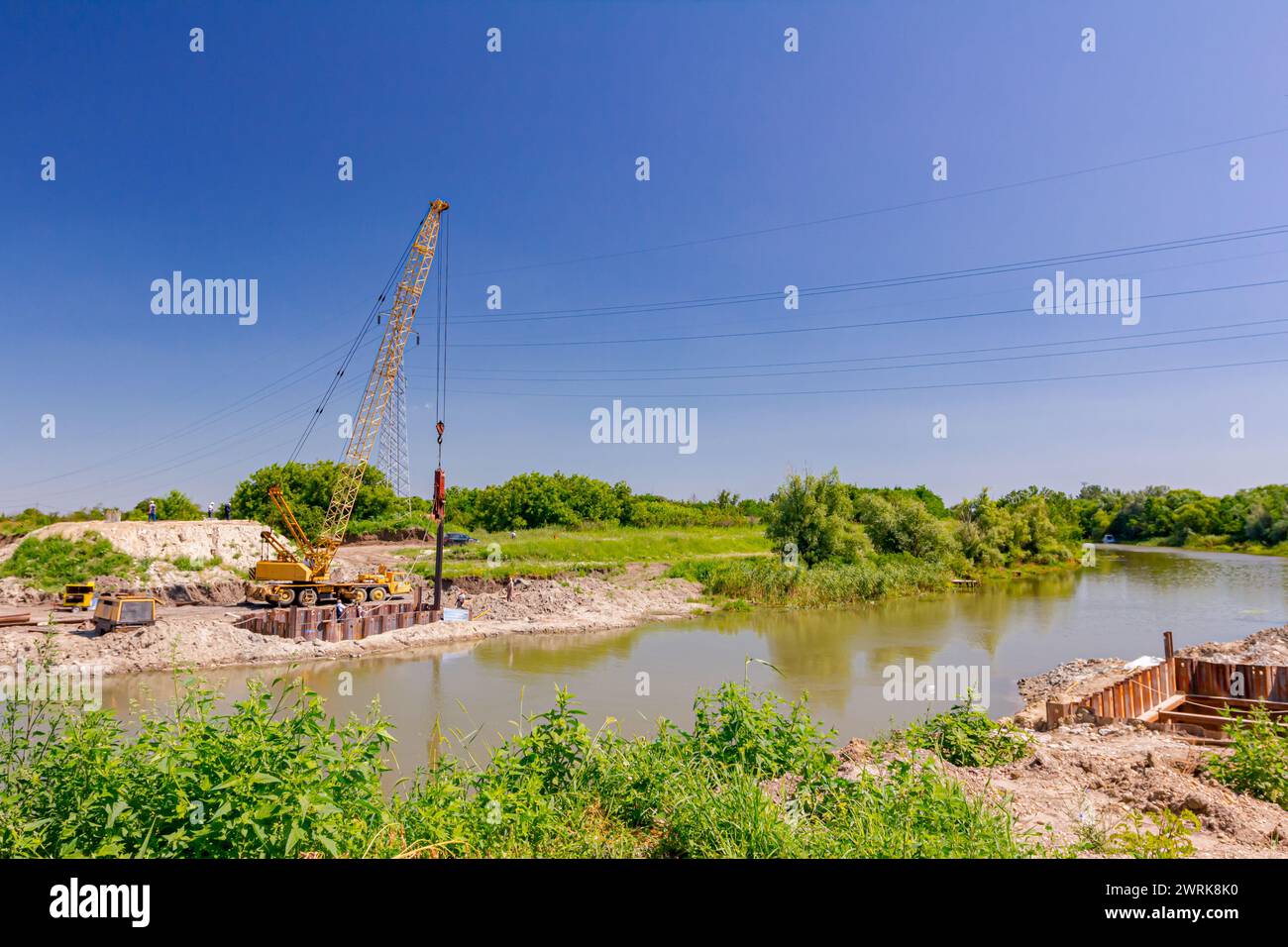 Across the water is yellow obsolete mobile crane with pneumatic hammer ...