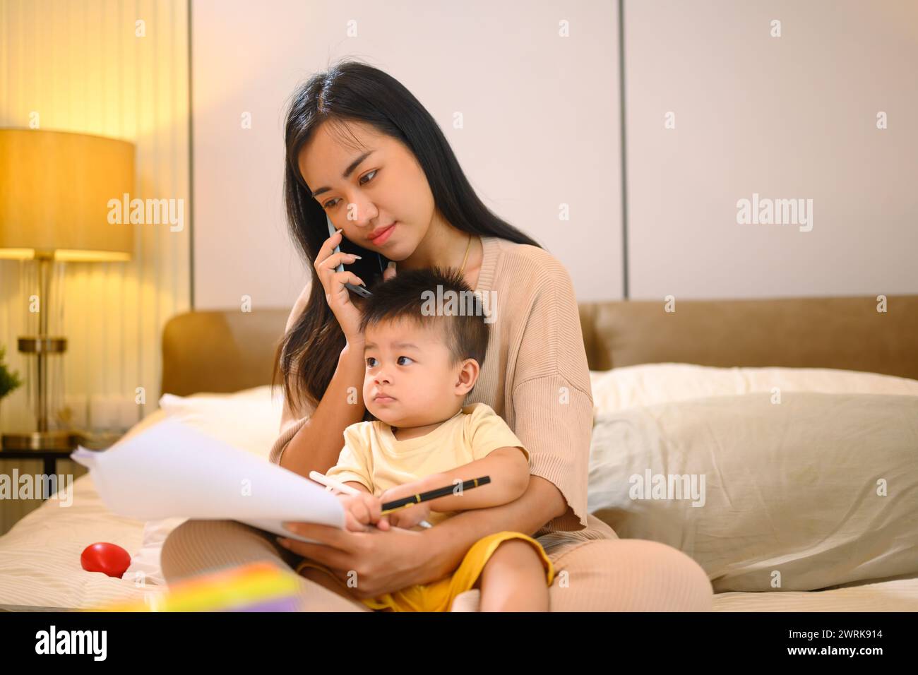 Busy working mom talking on mobile phone and holding her baby son ...