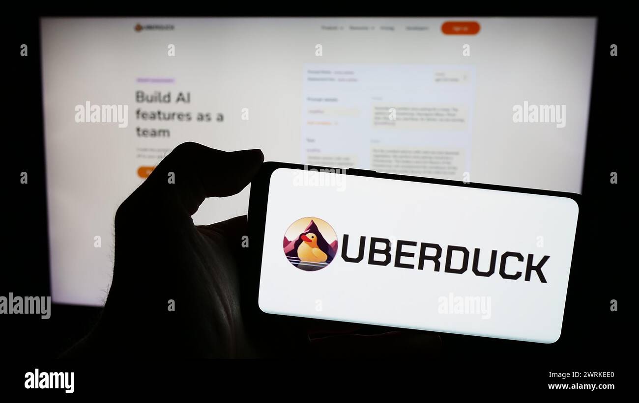 Person holding mobile phone with logo of US artificial intelligence music company Uberduck Inc ...