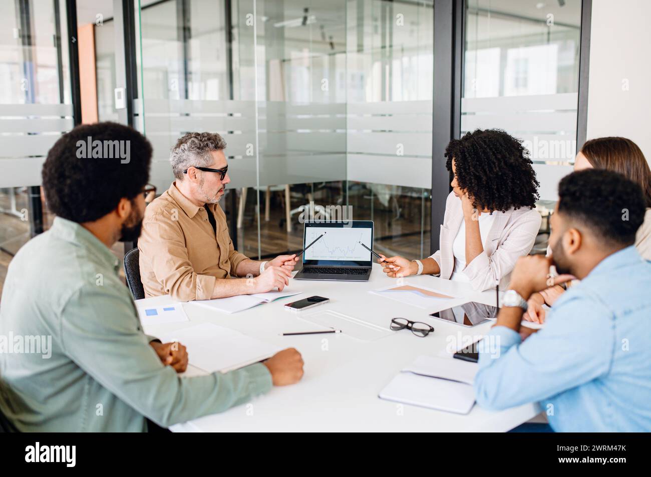 A diverse team is deeply engaged around a laptop, with a mature man ...