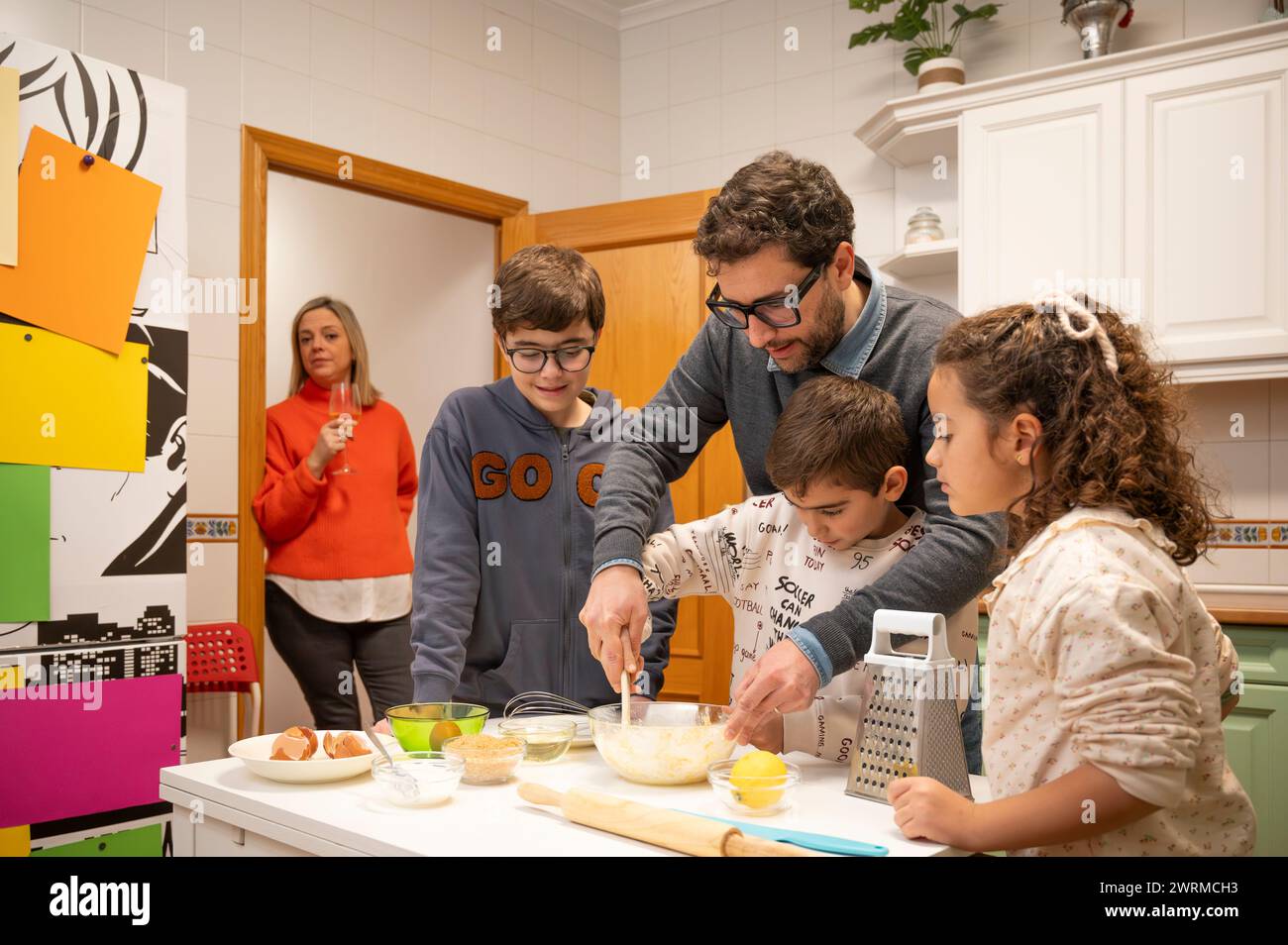 A family enjoys a cooking session together in a well-lit kitchen, with ...