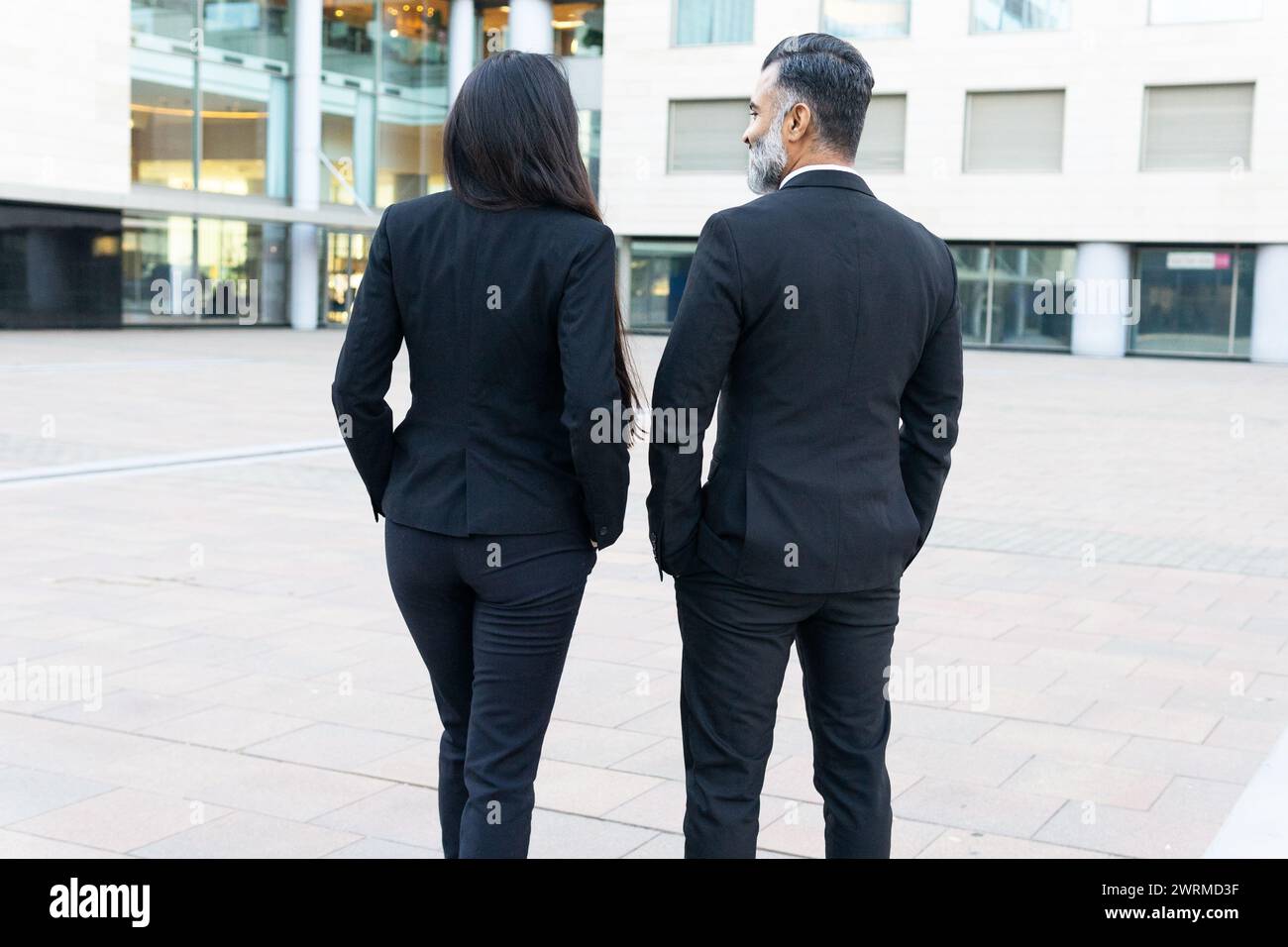 Back view of man and woman in professional attire walking together with a modern office building ...