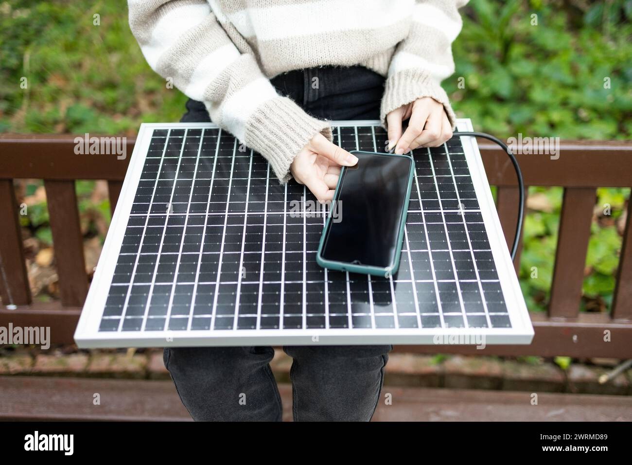 "Person outdoor using a solar panel to charge a smartphone, showcasing ...