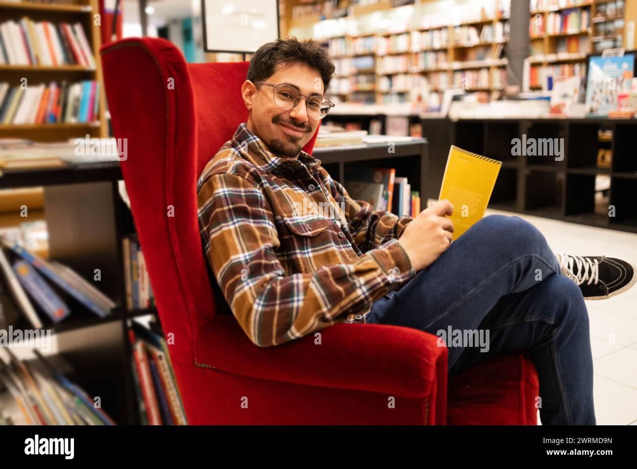 Side view of cheerful man enjoys reading a book while seated on a red ...