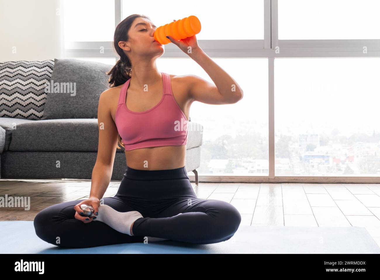 A young woman seated on a blue yoga mat in a Sukhasana pose, commonly ...