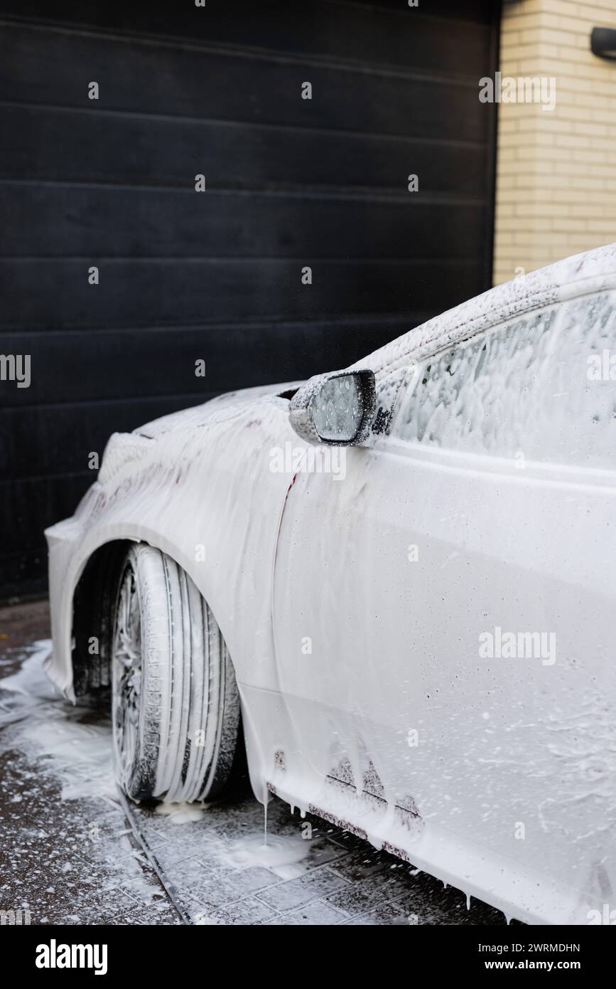 A close-up view of a white car being cleaned, covered in soap foam at ...