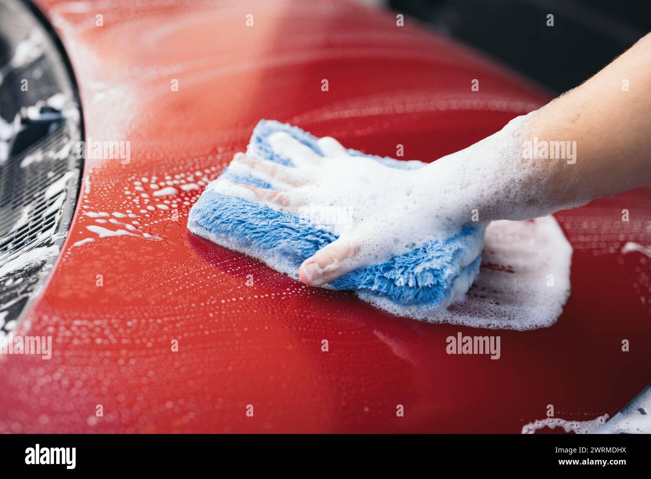 Hand washing a red car with a blue microfiber cloth and sudsy foam ...
