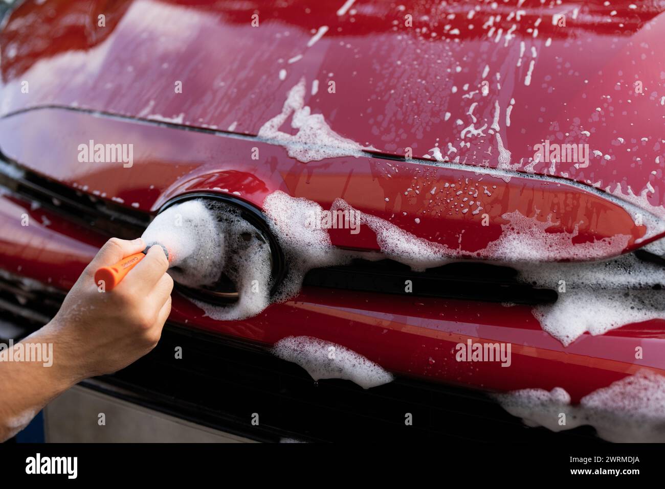Hand washing a red car with soapy water and a sponge focusing on the ...
