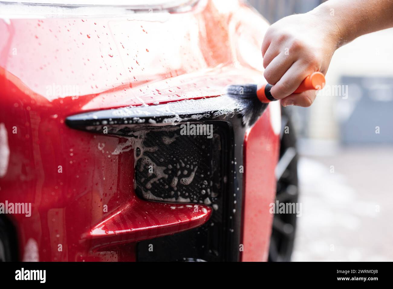 Hand washing a red car with detailer brush and soap suds on vehicle ...