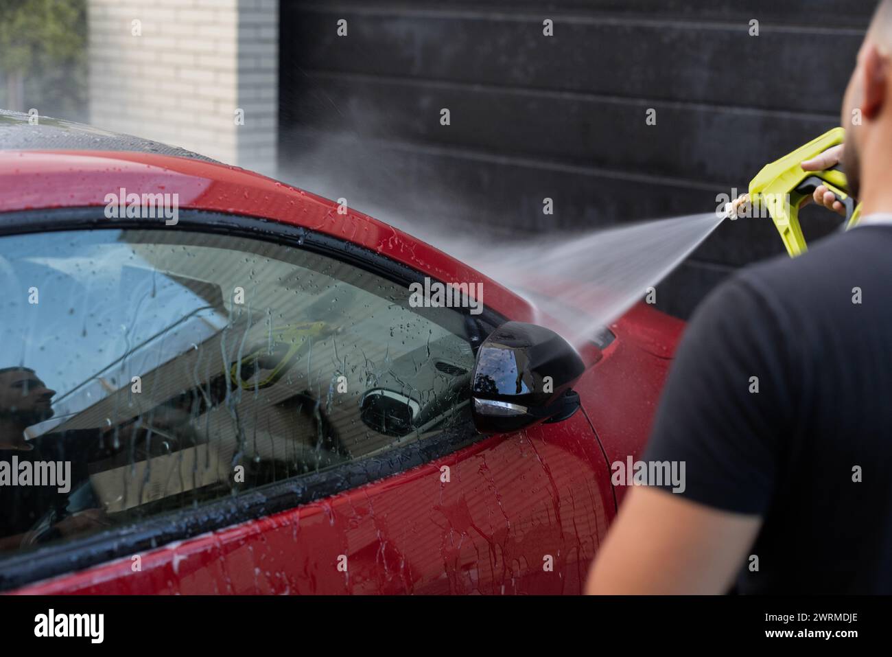 A person is using a high-pressure water spray to clean the side window ...
