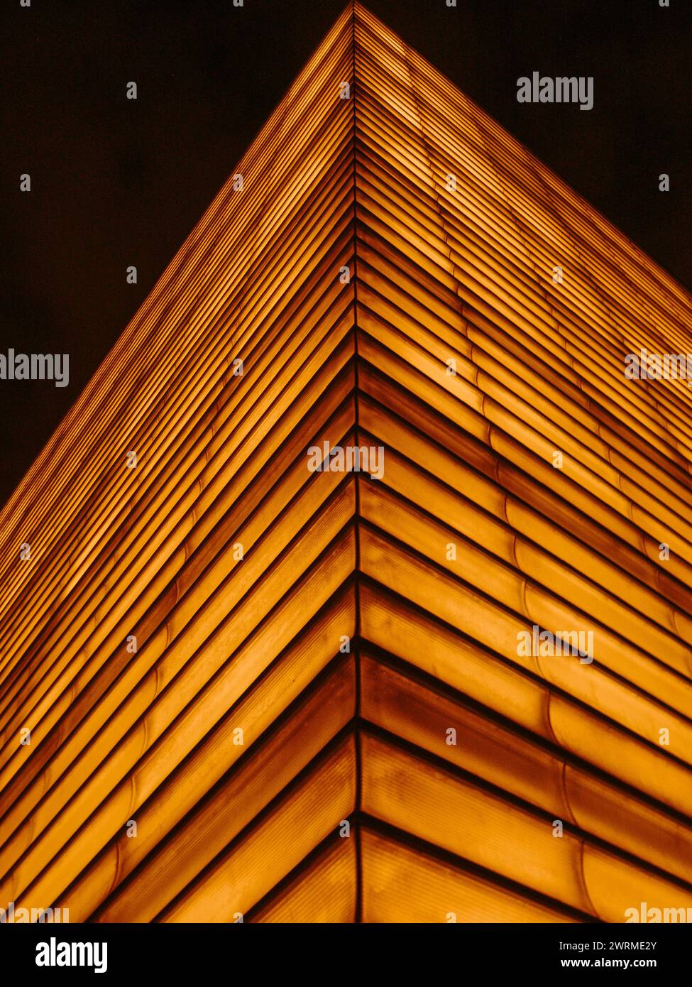 An abstract view of a golden-lit modern building facade at night ...