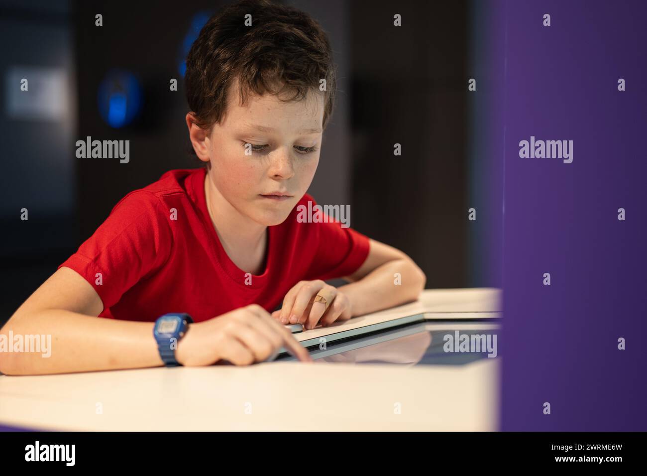 A thoughtful boy in a red shirt concentrates on an interactive exhibit ...