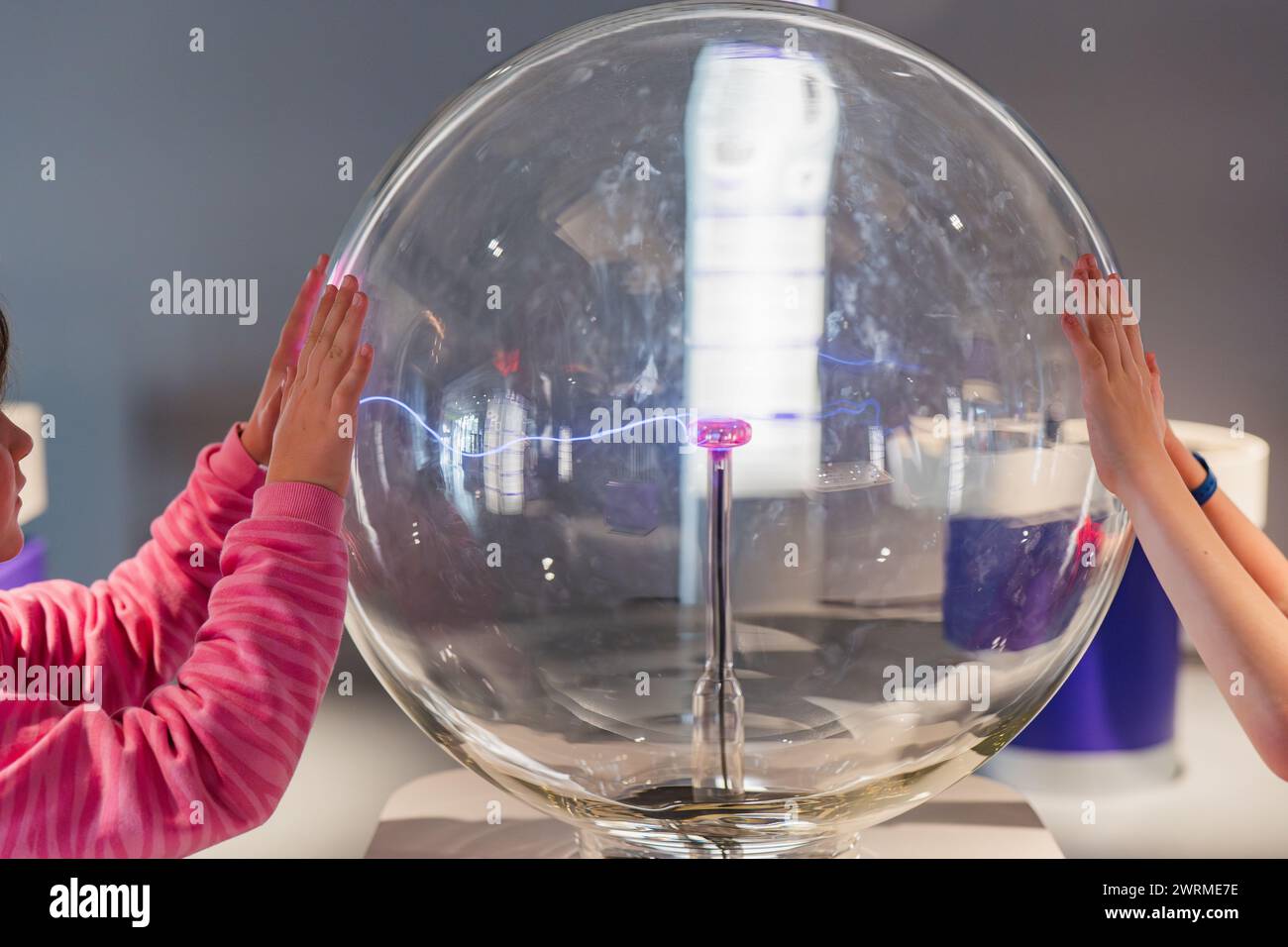 Boy and girl engaged with an interactive plasma globe exhibit at a science museum, showing ...