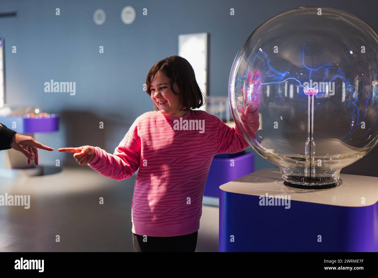 Young girl enjoys a hands-on learning experience with a plasma globe at a science museum ...