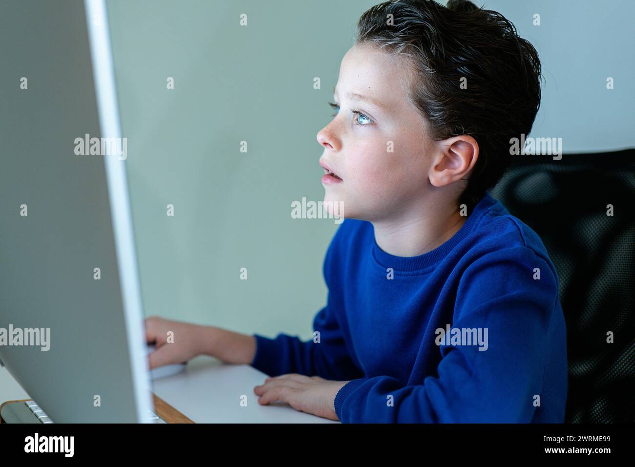 A young boy with a look of concentration while using a computer in a ...