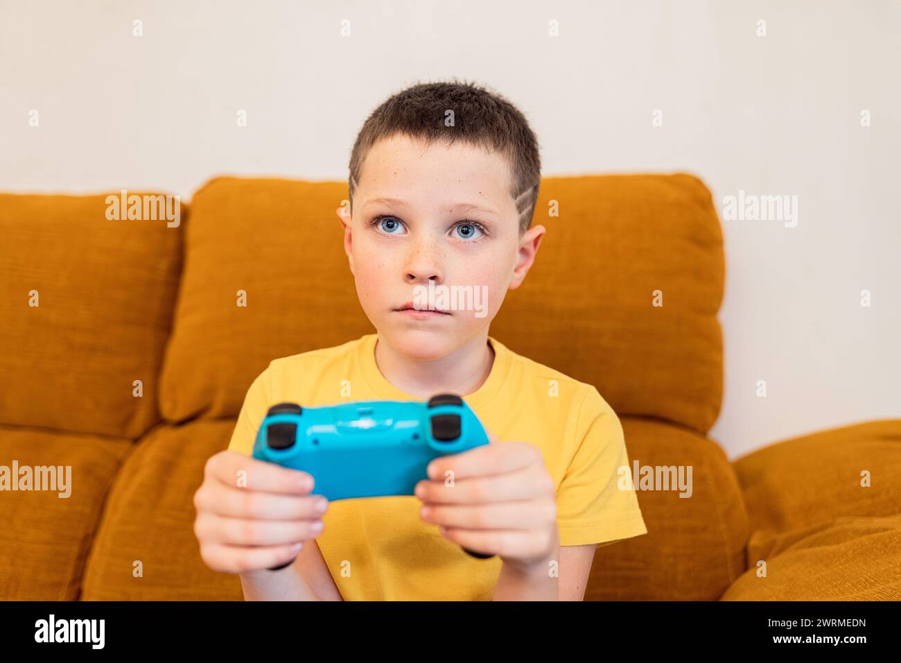 A focused young boy plays video games while holding a blue controller ...