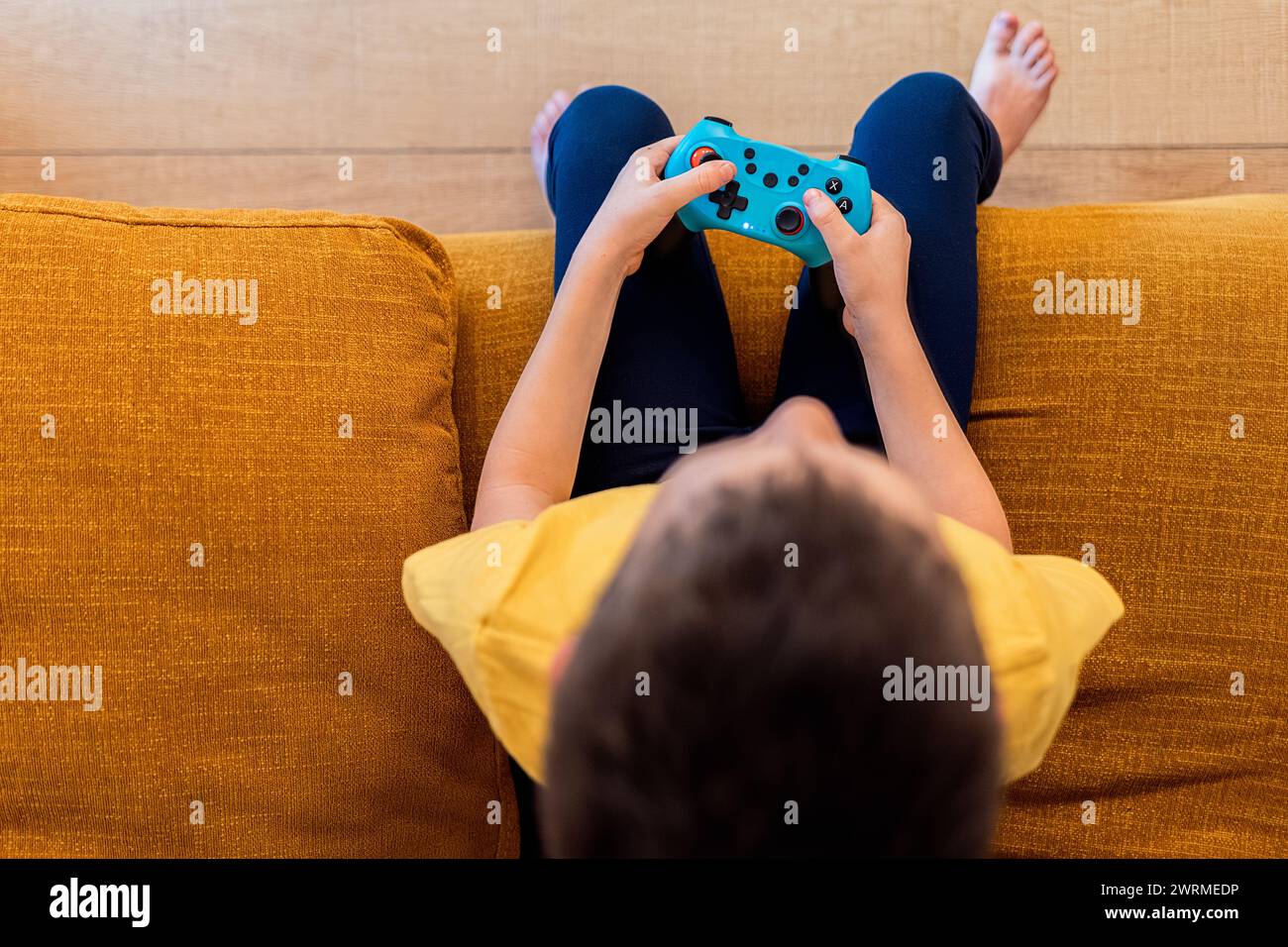 Overhead view of a child sitting on a sofa, playing video games with a ...