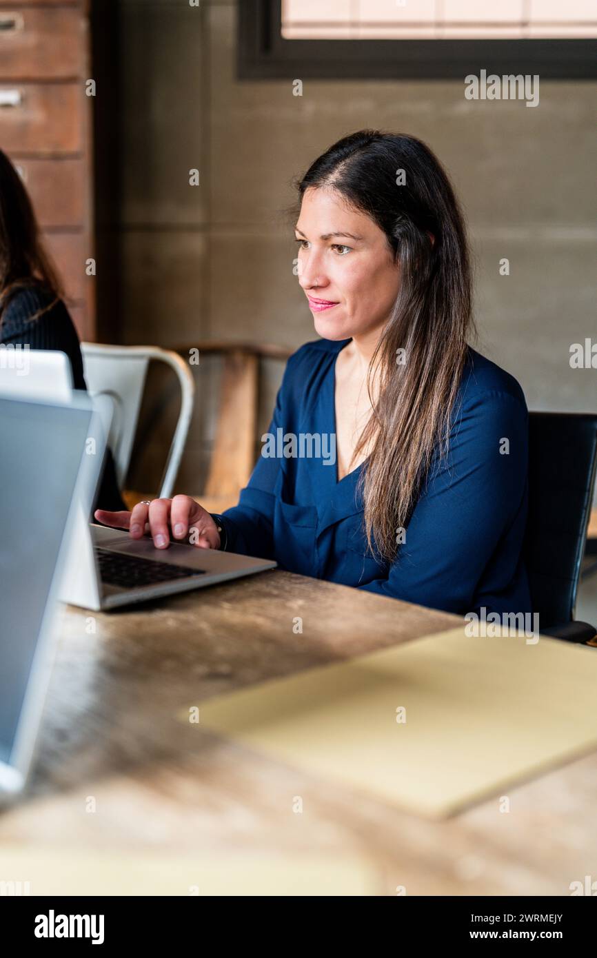 A woman focused on her laptop while working from a cafe, representing a ...
