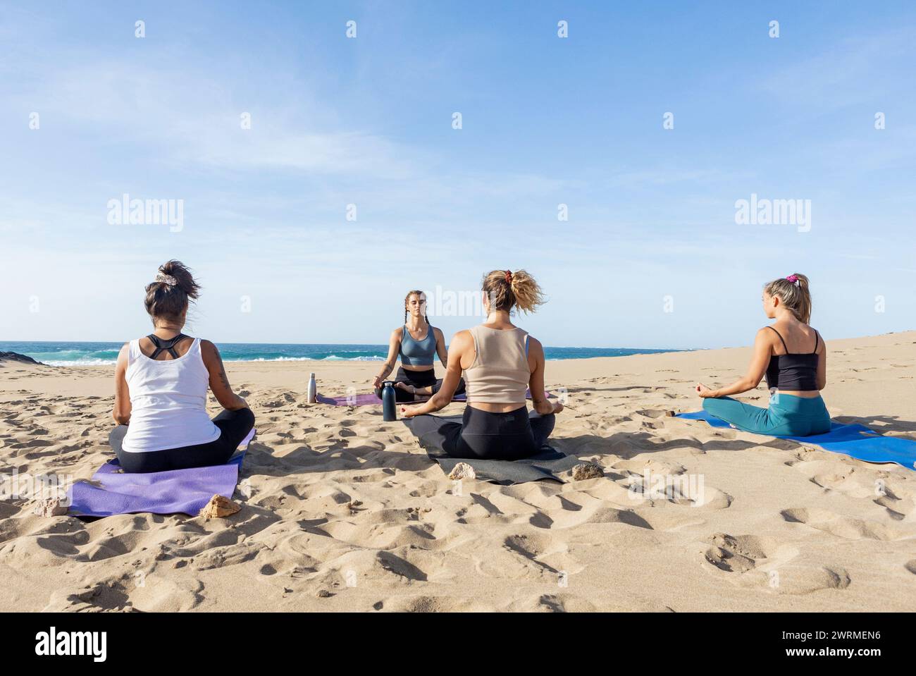 A group of women participate in a calming yoga class on the sand, with ...